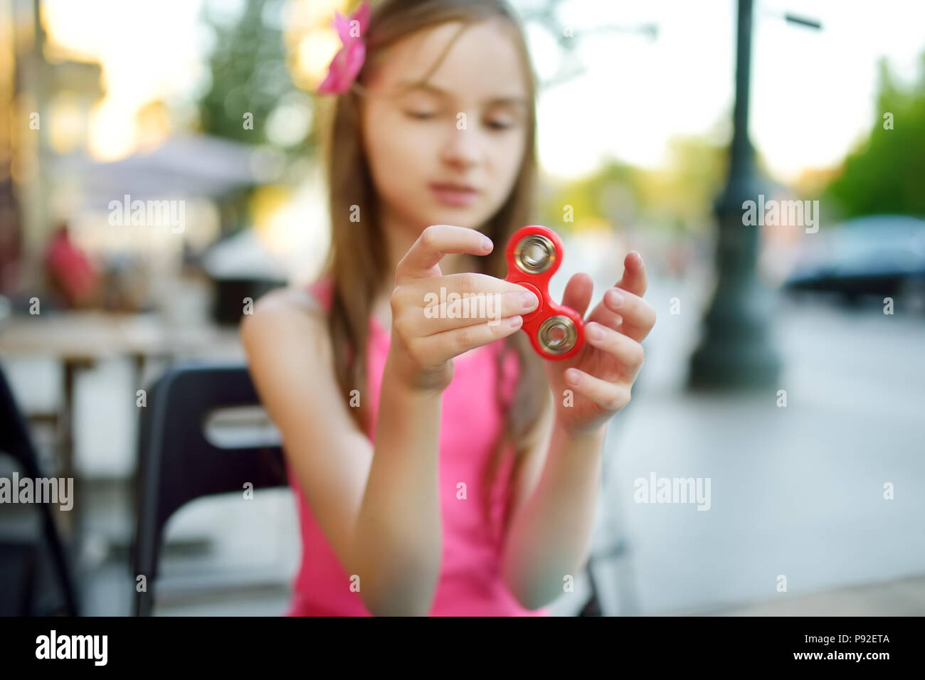 Cute school girl playing with colorful fidget spinner in outdoor cafe ...