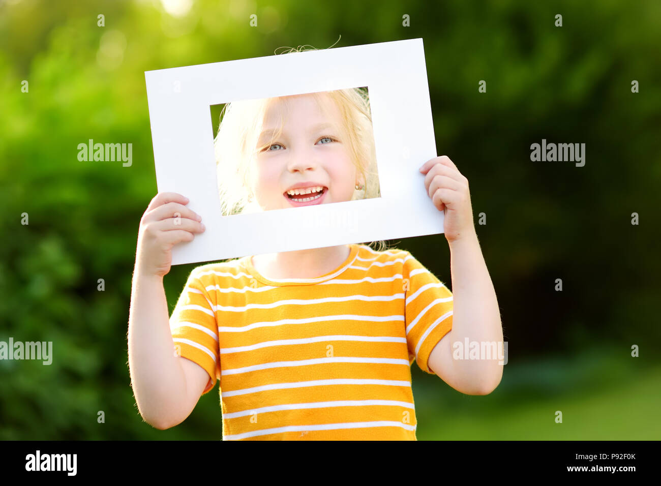 Cute cheerful little girl holding white picture frame in front of her ...