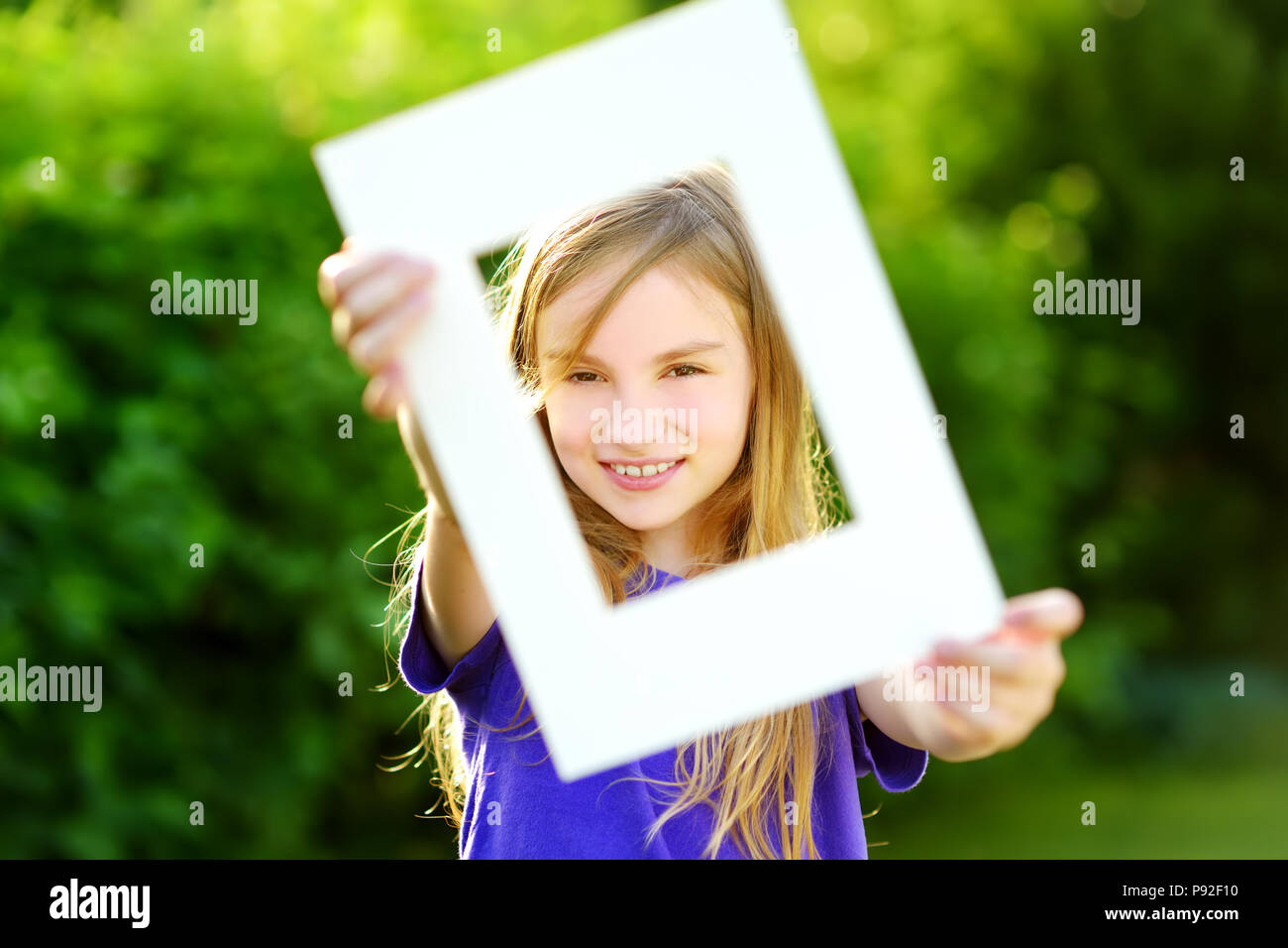 Cute cheerful little girl holding white picture frame in front of her ...