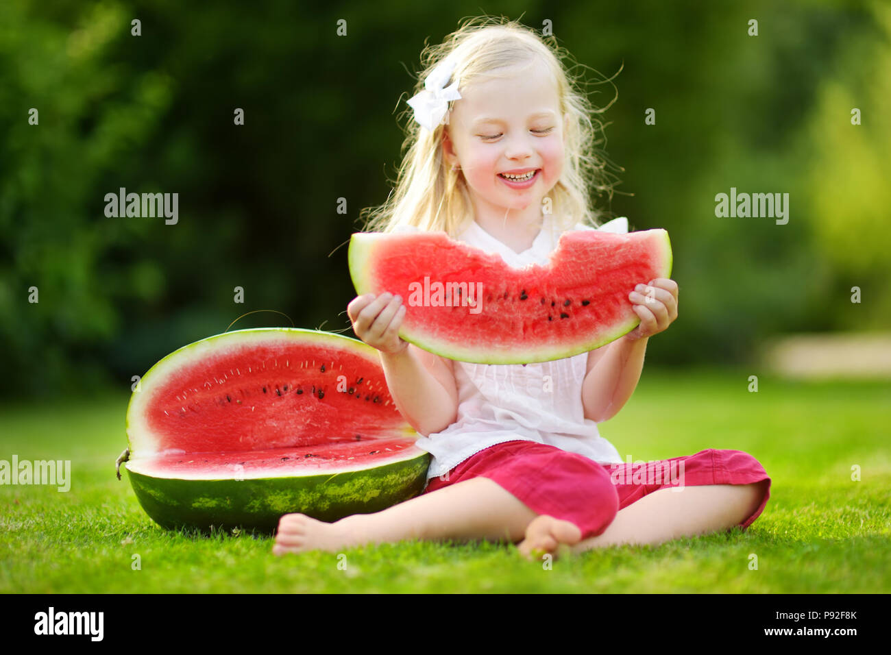Funny little girl biting a slice of watermelon outdoors on warm and ...