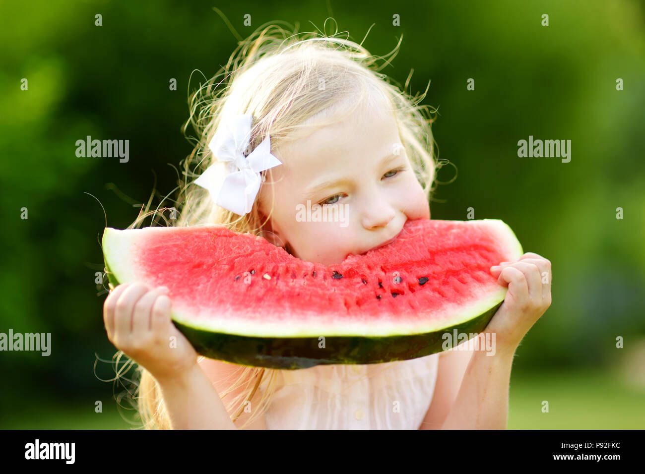 Funny little girl biting a slice of watermelon outdoors on warm and ...