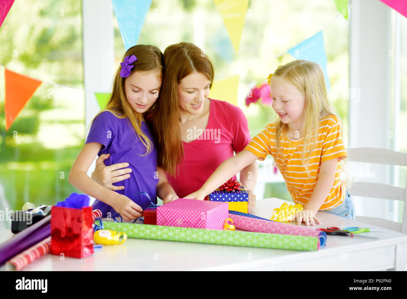 Two cute sisters and their young mother wrapping gifts in colorful ...