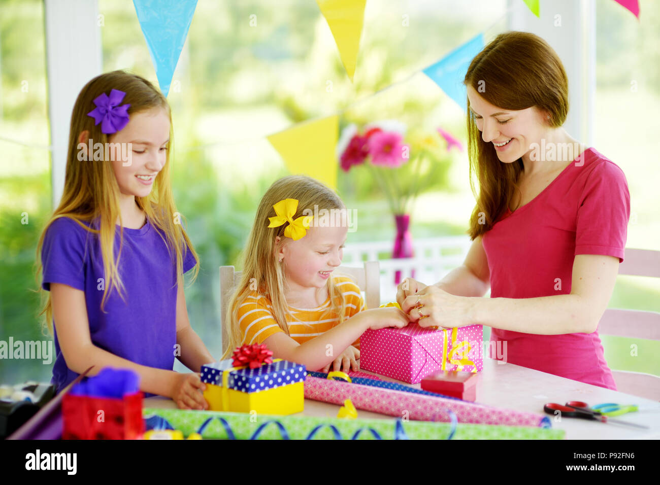Two cute sisters and their young mother wrapping gifts in colorful ...