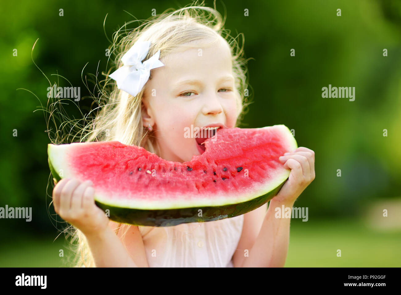 Funny little girl biting a slice of watermelon outdoors on warm and ...