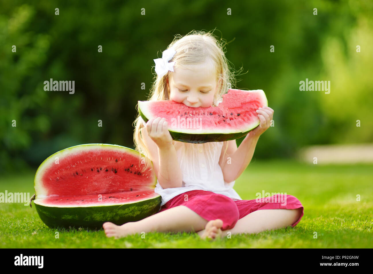 Funny little girl biting a slice of watermelon outdoors on warm and ...