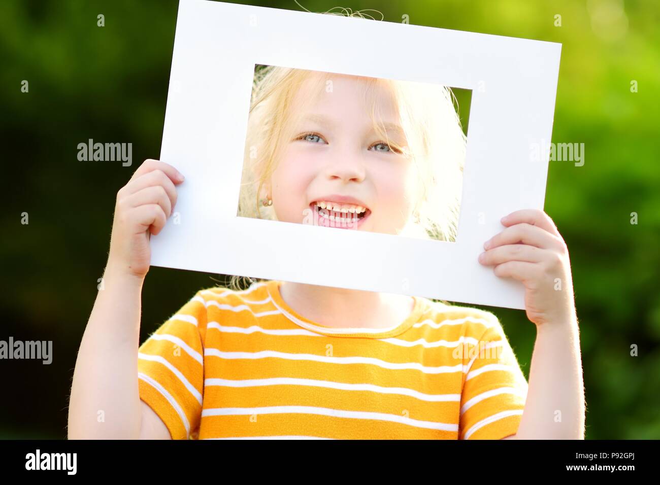 Cute cheerful little girl holding white picture frame in front of her ...