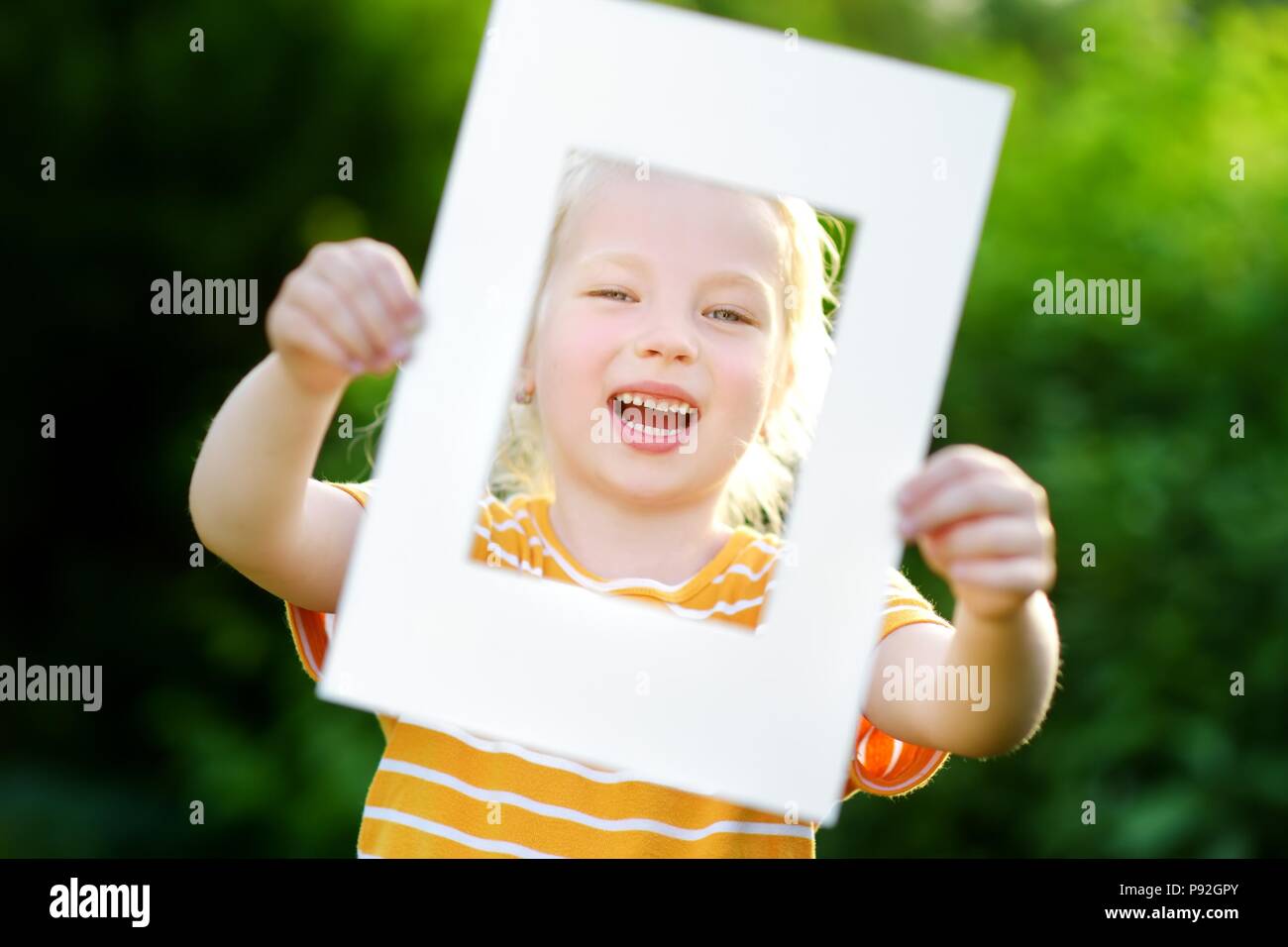 Cute cheerful little girl holding white picture frame in front of her ...