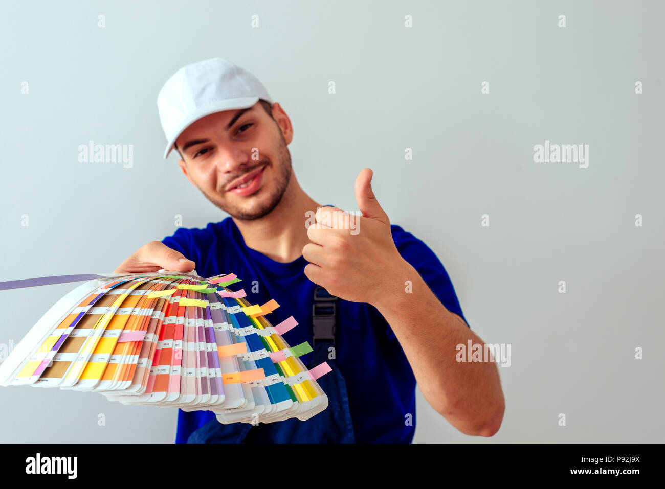 Young worker with thumbs up is holding color guide for wall Stock Photo ...