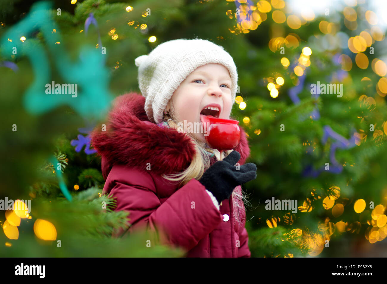 Adorable little girl eating red apple covered with sugar icing on ...