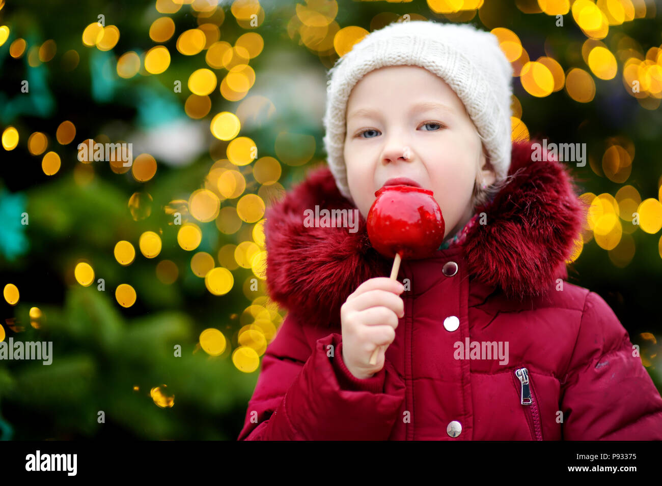 Adorable little girl eating red apple covered with sugar icing on ...