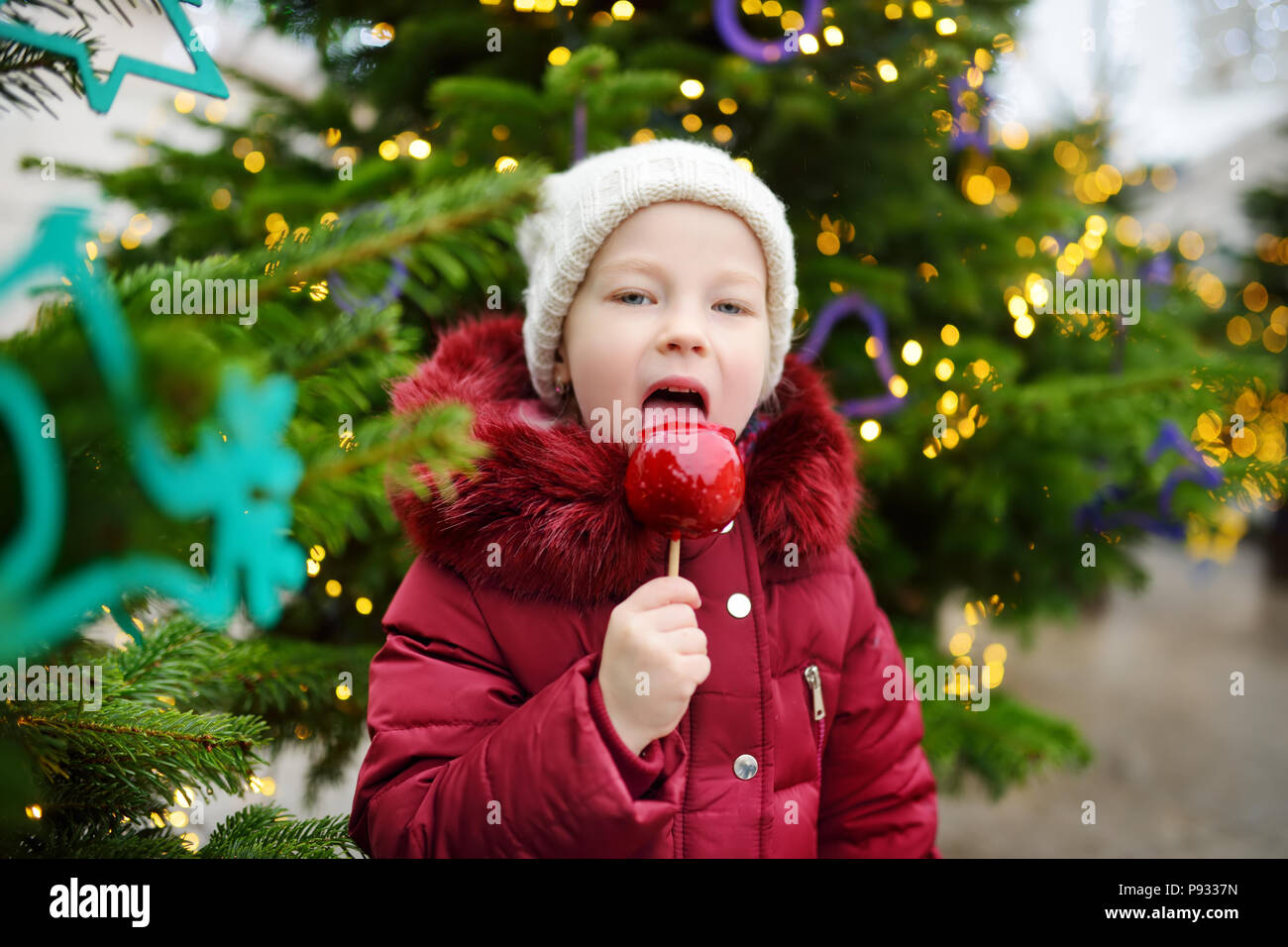 Adorable little girl eating red apple covered with sugar icing on ...