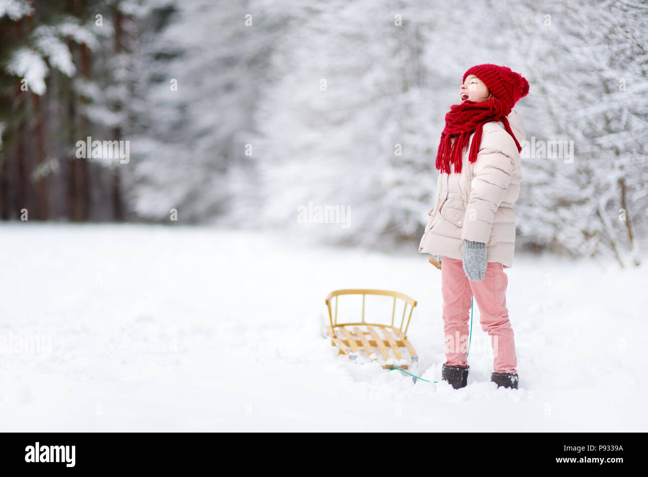 Funny little girl having fun with a sleight in beautiful winter park ...