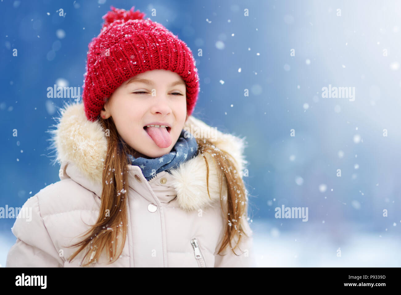 Adorable little girl catching snowflakes with her tongue in beautiful ...