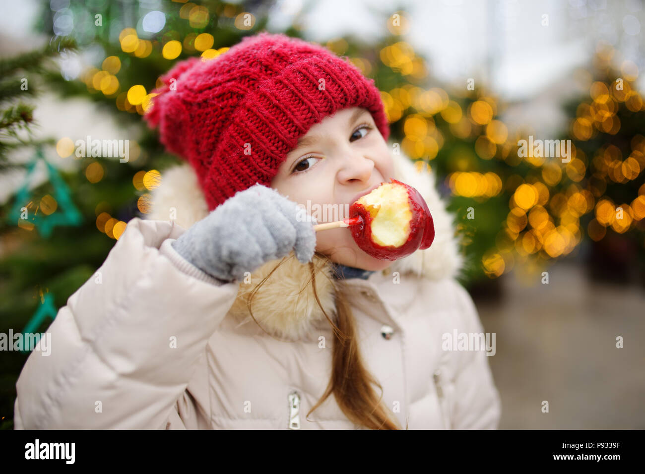 Adorable little girl eating red apple covered with sugar icing on ...