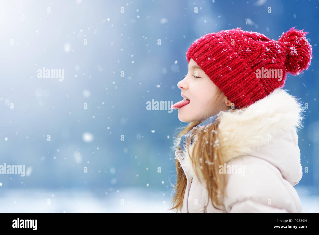 Adorable little girl catching snowflakes with her tongue in beautiful ...