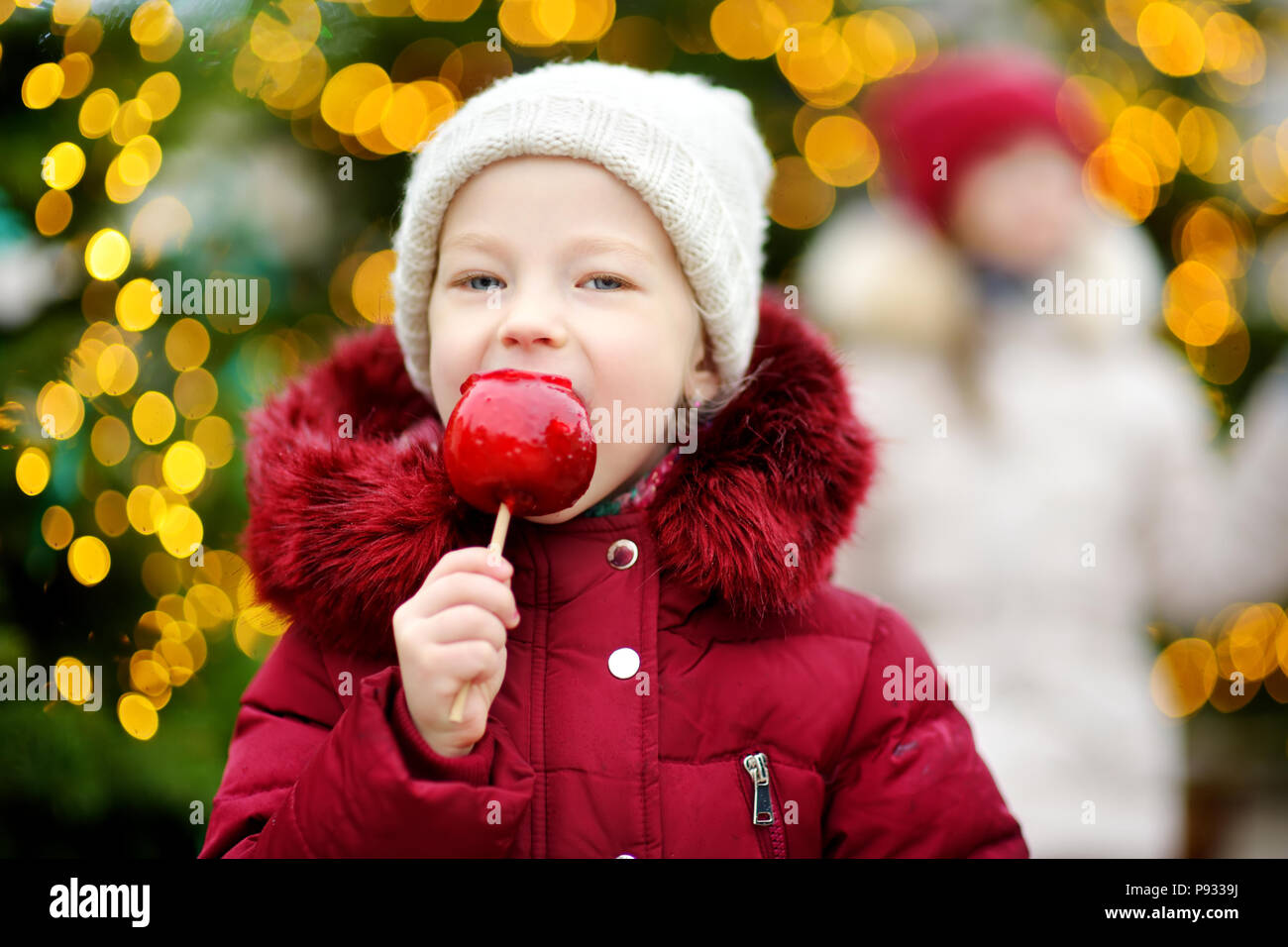 Adorable little girl eating red apple covered with sugar icing on ...