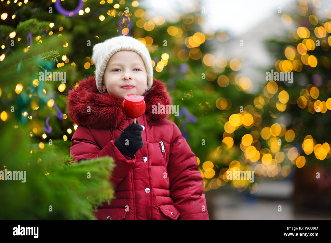 Adorable little girl eating red apple covered with sugar icing on ...