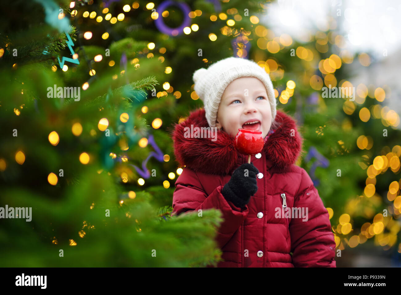 Adorable little girl eating red apple covered with sugar icing on ...