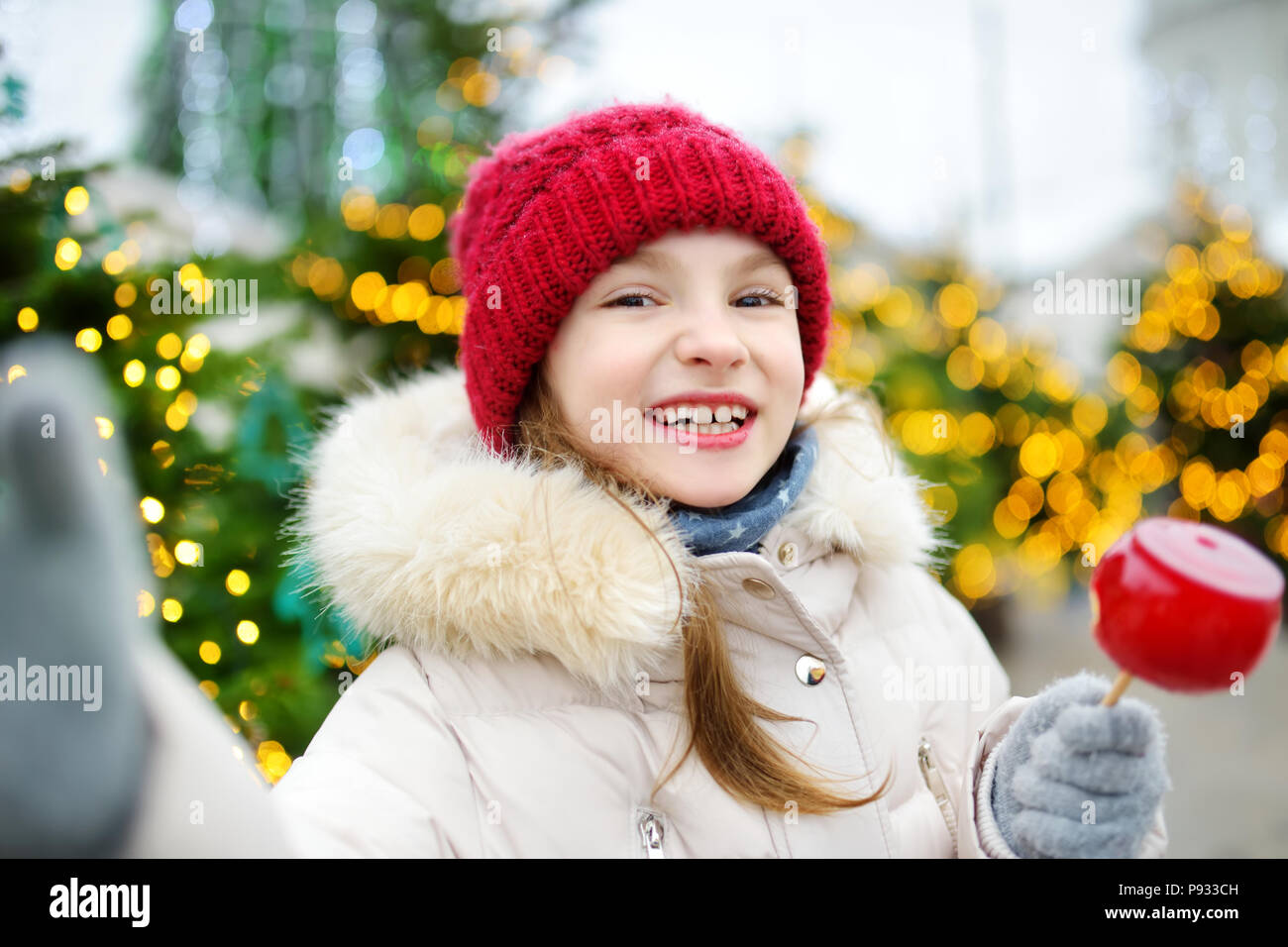 Adorable little girl eating red apple covered with sugar icing on ...