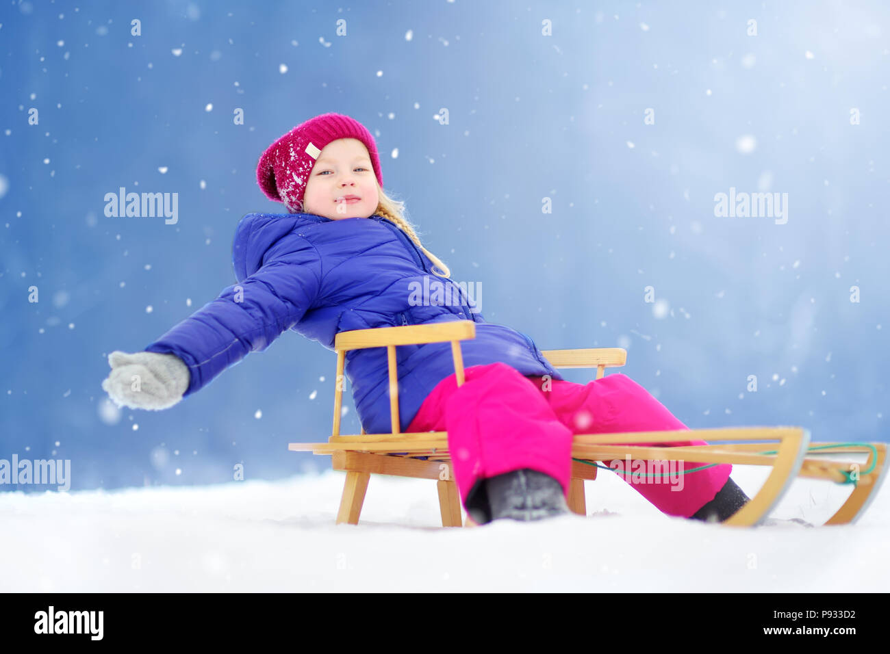 Funny little girl having fun with a sleight in beautiful winter park ...