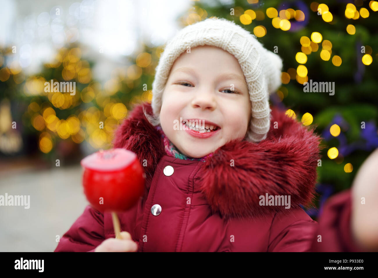 Adorable little girl eating red apple covered with sugar icing on ...