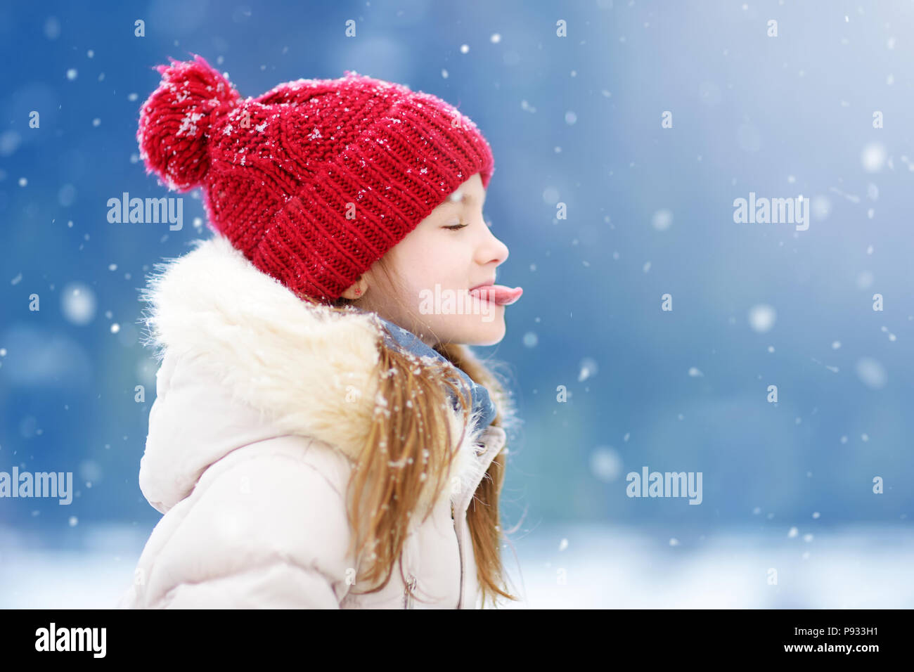 Adorable little girl catching snowflakes with her tongue in beautiful ...