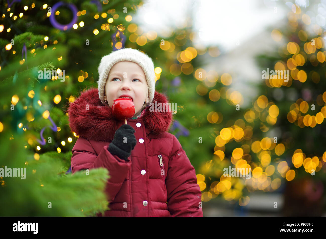 Adorable little girl eating red apple covered with sugar icing on ...