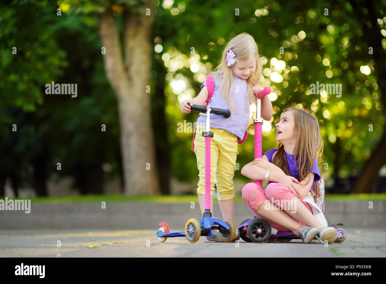 Small children learning to ride scooters in a city park on sunny summer ...