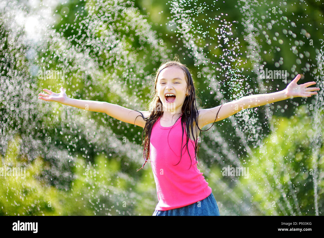 Adorable little girl playing with a sprinkler in a backyard on sunny ...