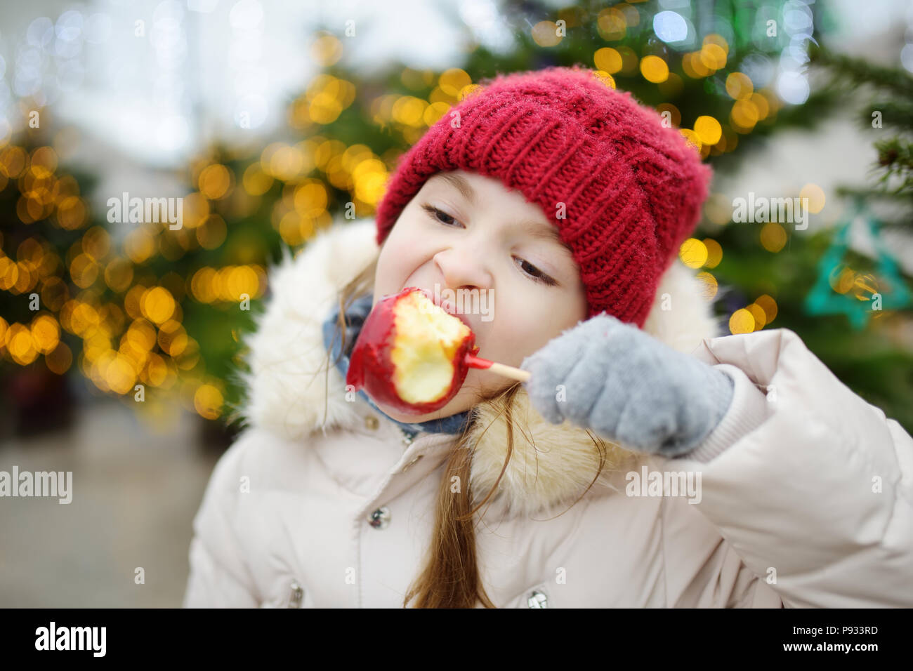 Adorable little girl eating red apple covered with sugar icing on ...
