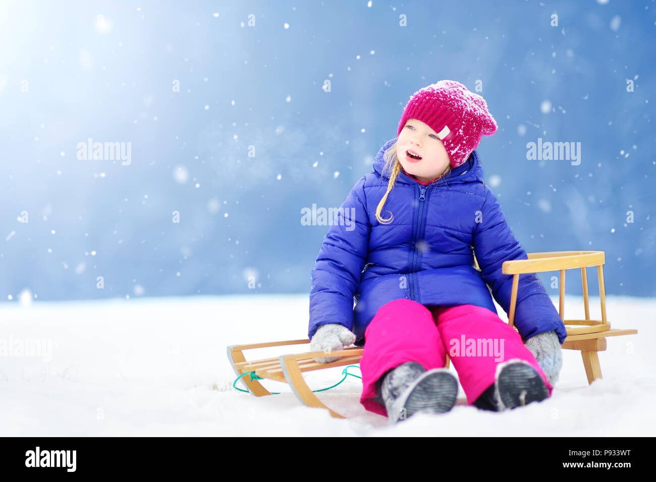 Funny little girl having fun with a sleight in beautiful winter park ...