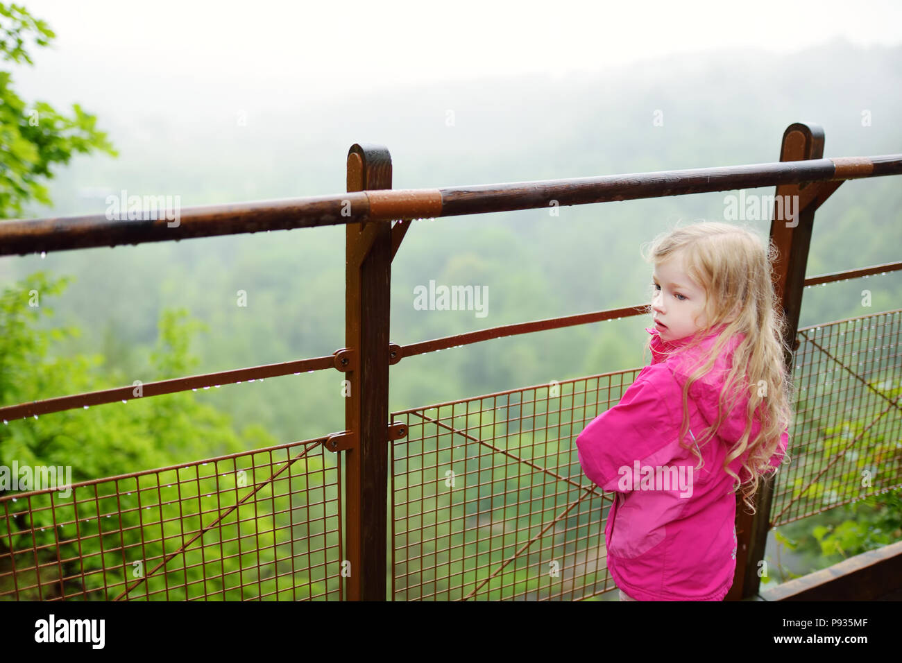 Adorable little girl playing happily in the rain on warm summer day ...