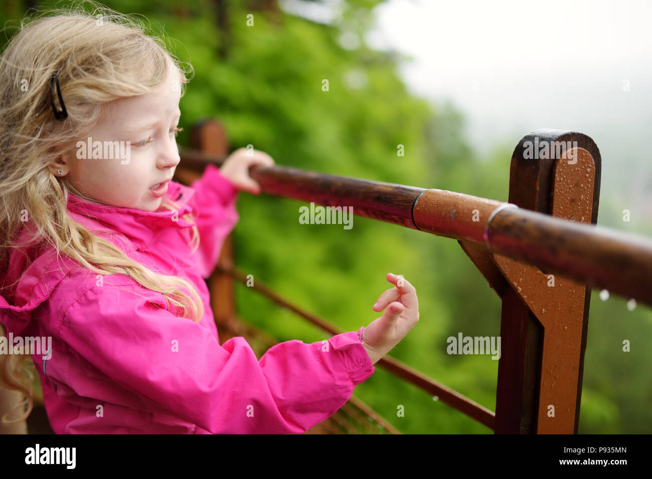 Adorable little girl playing happily in the rain on warm summer day ...