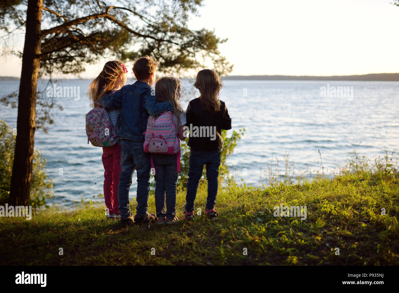 Four cute little sibling standing by the lake enjoying beautiful sunset ...