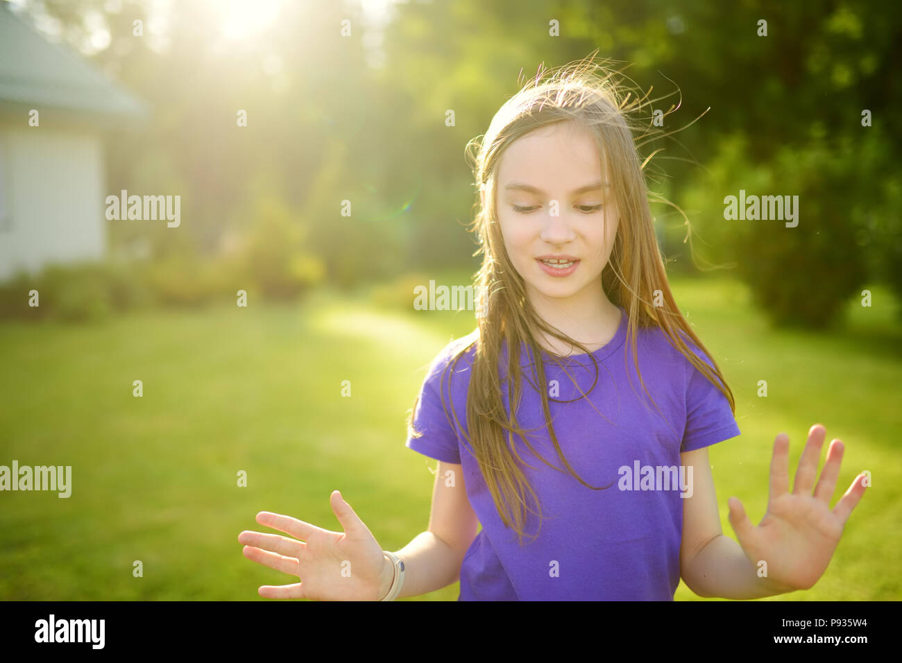 Cute little girl having fun on a grass on the backyard on sunny summer evening. Summer ...