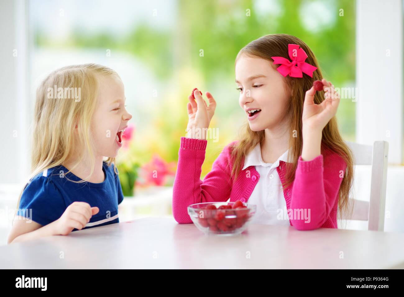Two pretty little girls eating raspberries at home. Cute children ...