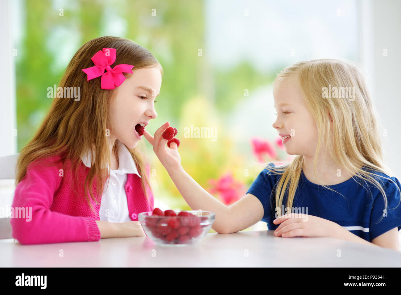 Two pretty little girls eating raspberries at home. Cute children ...