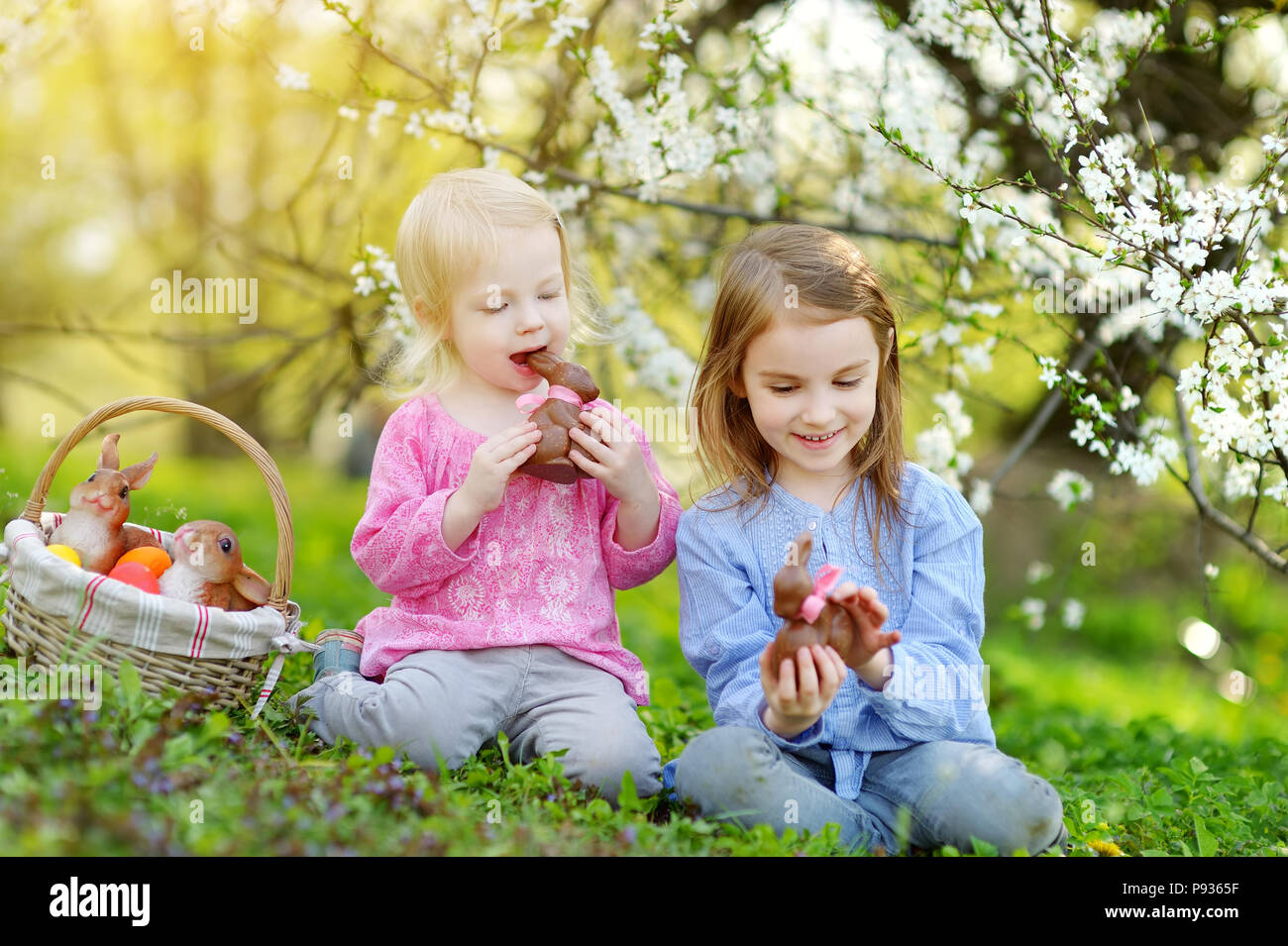 Two adorable little sisters eating chocolate bunnies in a spring garden ...