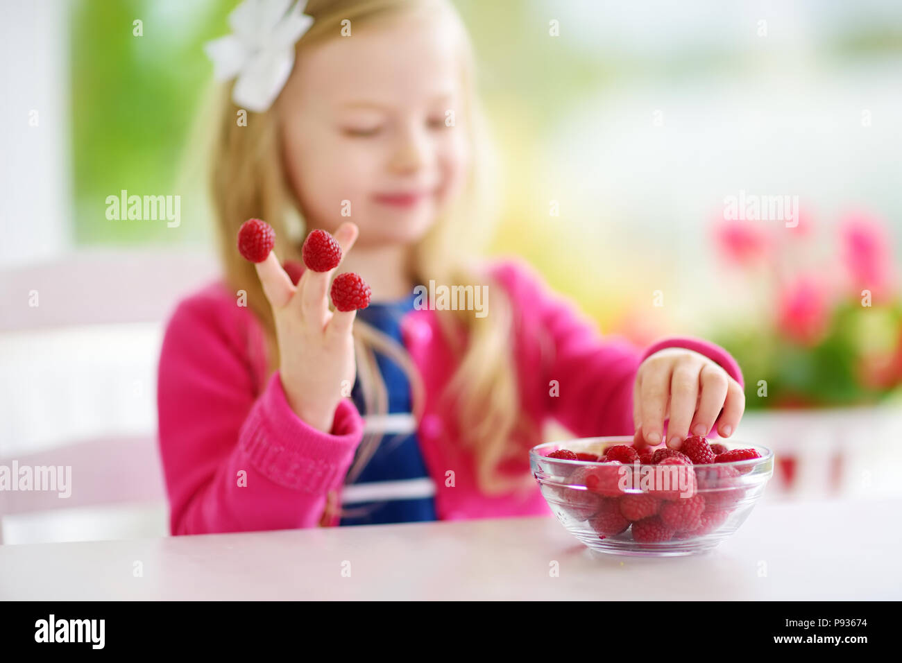 Pretty little girl eating raspberries at home. Cute child enjoying her ...