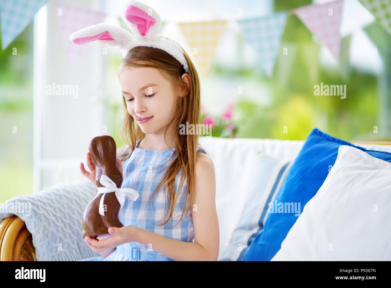 Cute little girl wearing bunny ears eating chocolate Easter rabbit. Kid ...