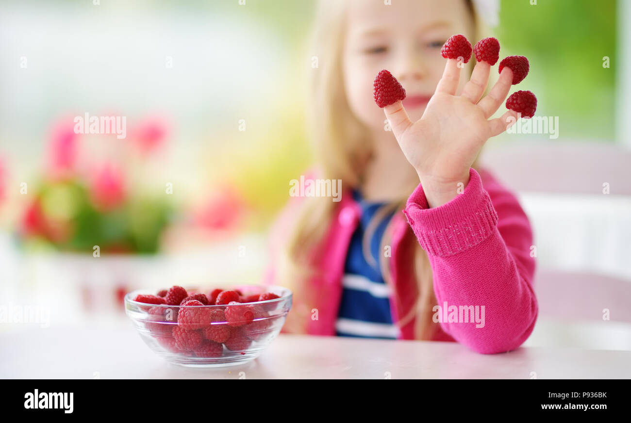 Pretty little girl eating raspberries at home. Cute child enjoying her ...