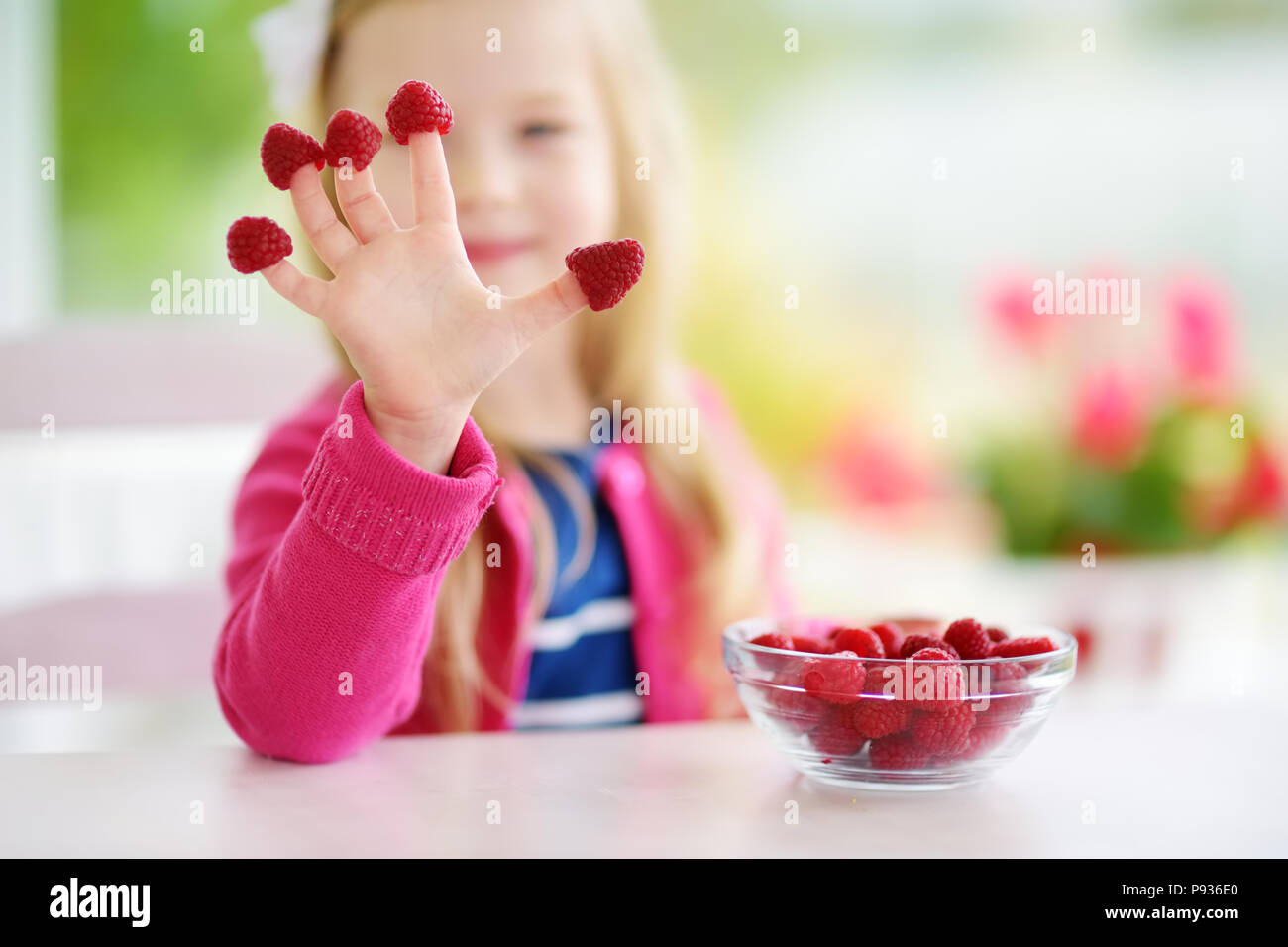 Pretty little girl eating raspberries at home. Cute child enjoying her ...