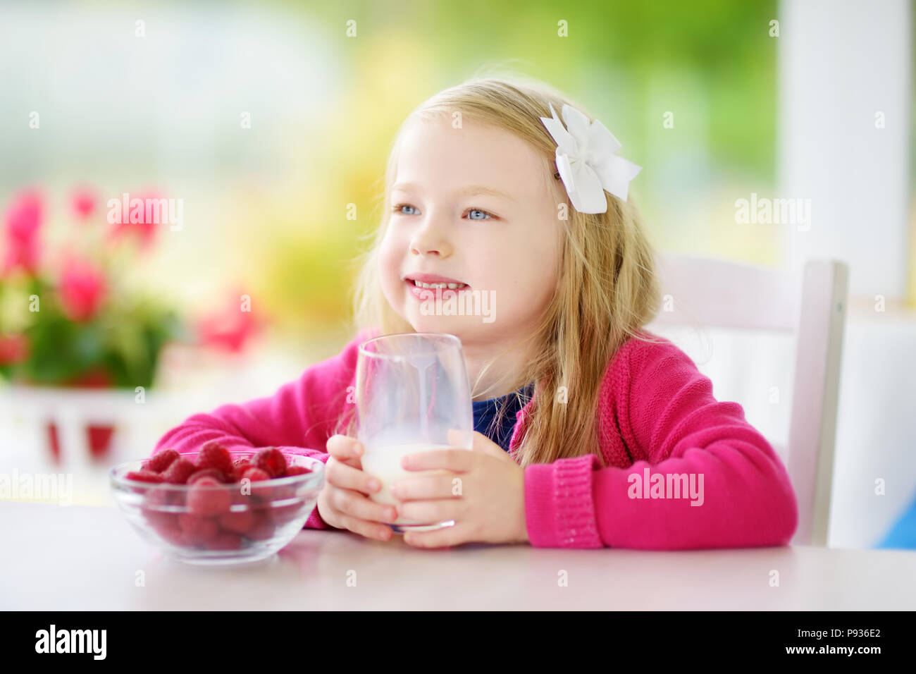 Pretty little girl eating raspberries and drinking milk at home. Cute ...