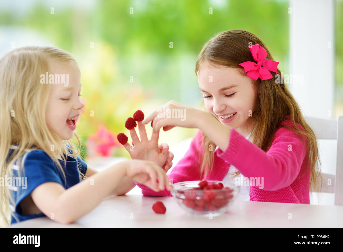 Two pretty little girls eating raspberries at home. Cute children ...