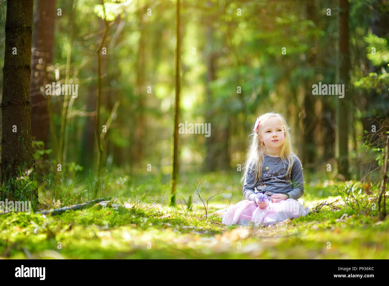 Adorable little girl picking the first flowers of spring in the woods ...