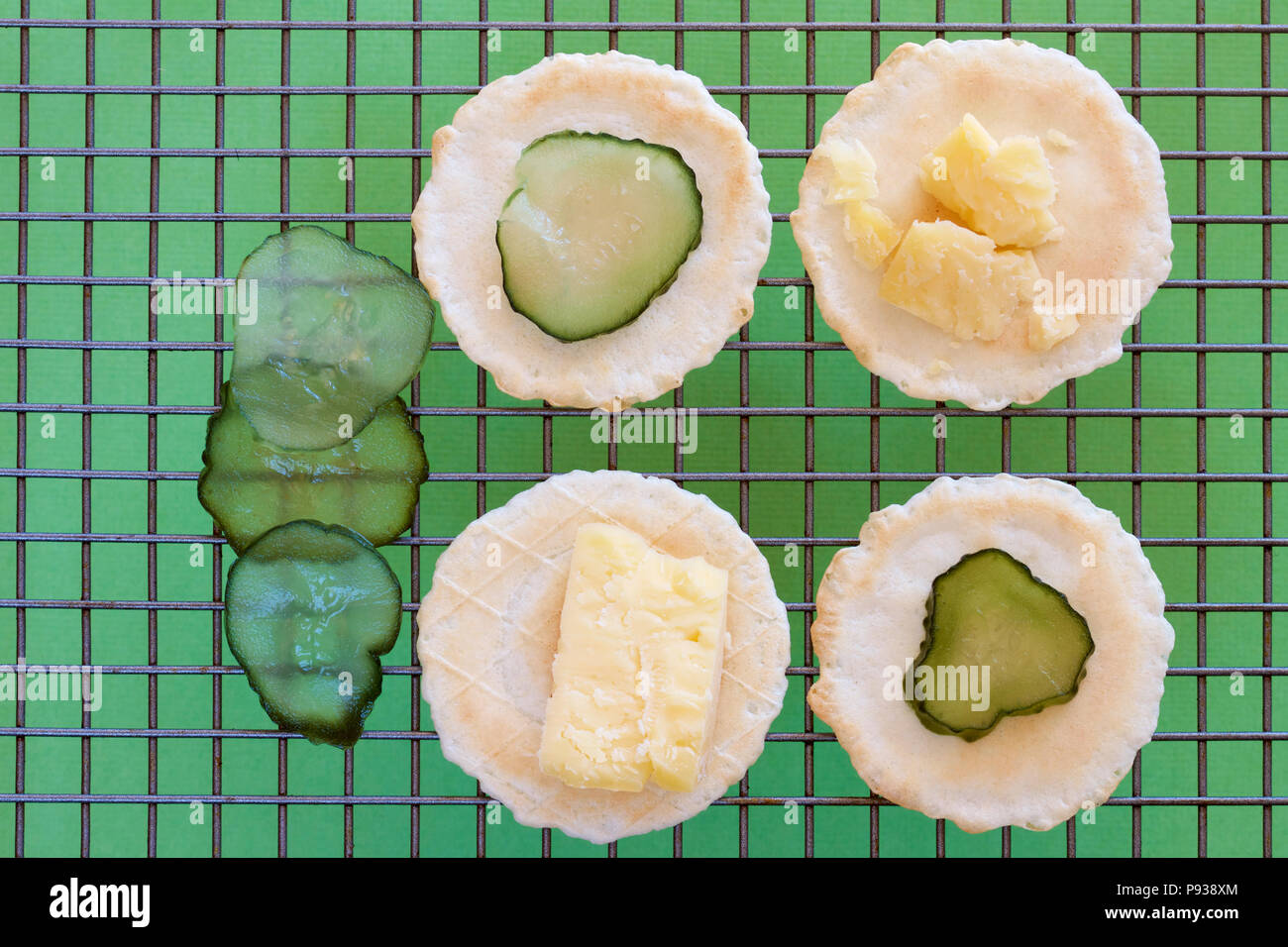 Gherkin slices and cheese on savoury biscuits on a grate with a green ...