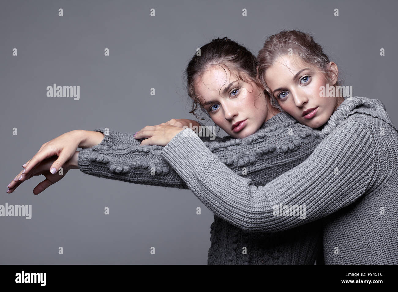 Two young women in gray sweaters on grey studio background. Beautiful ...