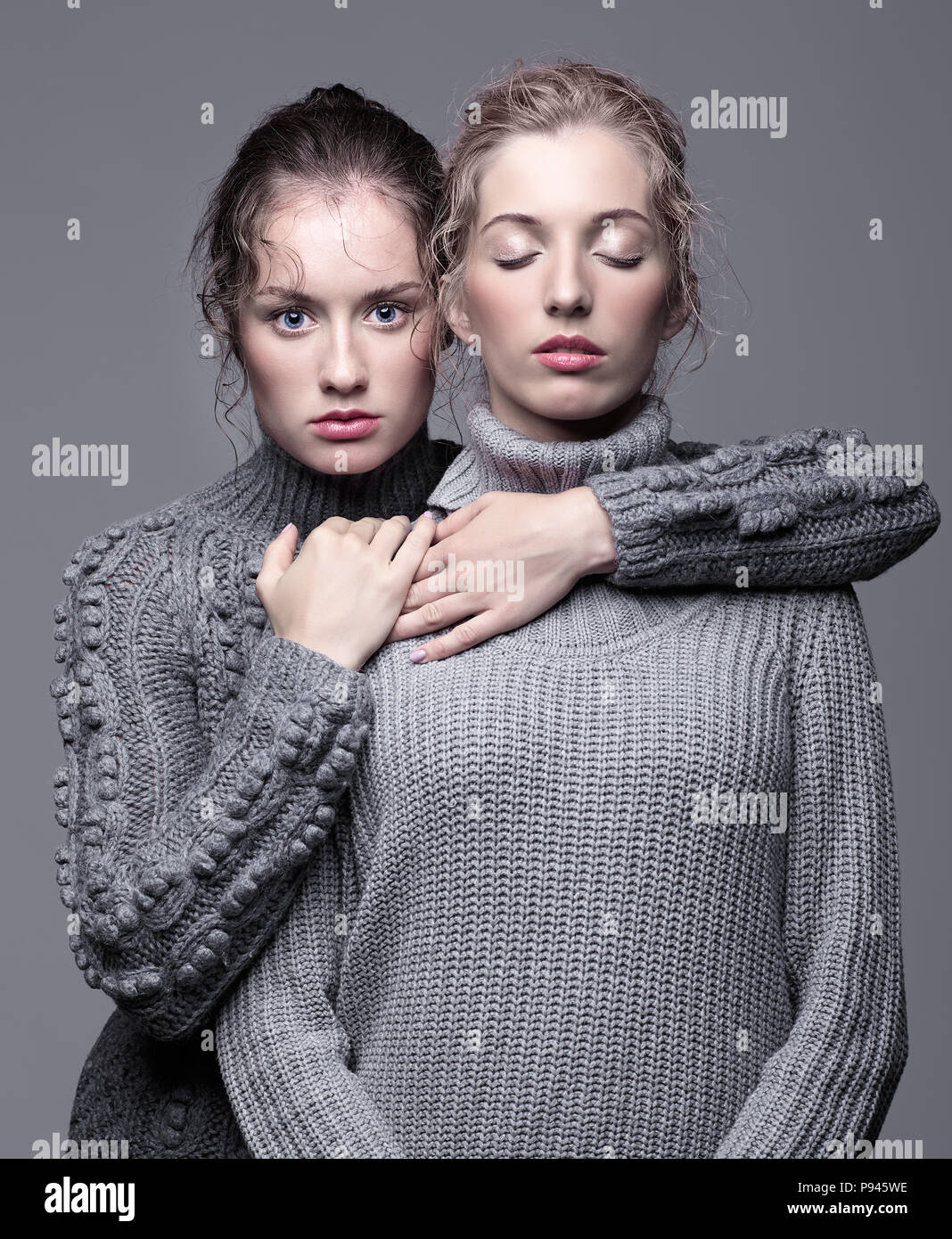 Two young women in gray sweaters on grey studio background. Beautiful ...