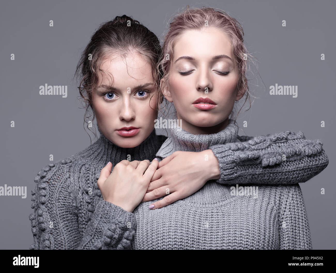 Two young women in gray sweaters on grey studio background. Beautiful ...