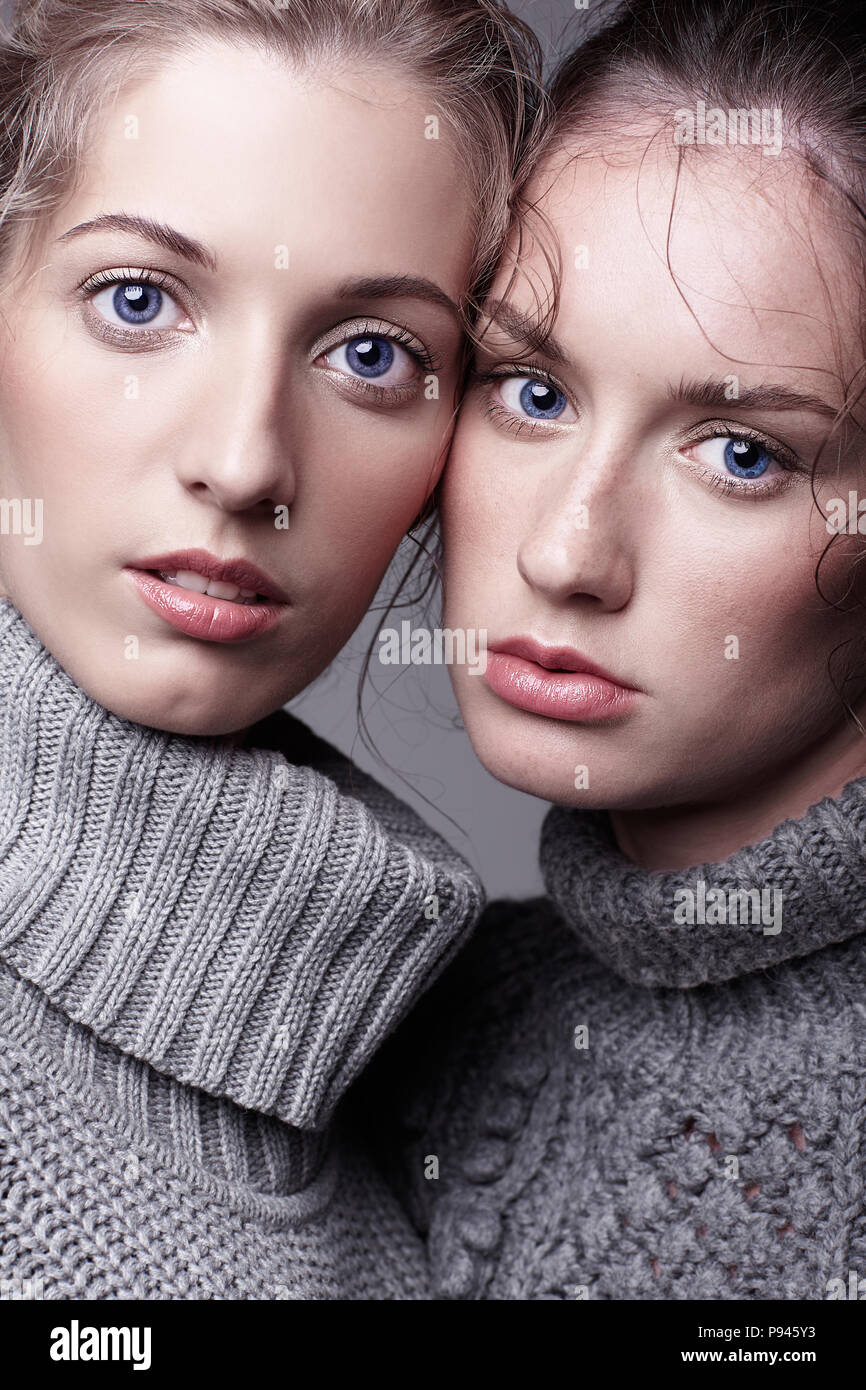 Two young women in gray sweaters on grey studio background. Beautiful ...